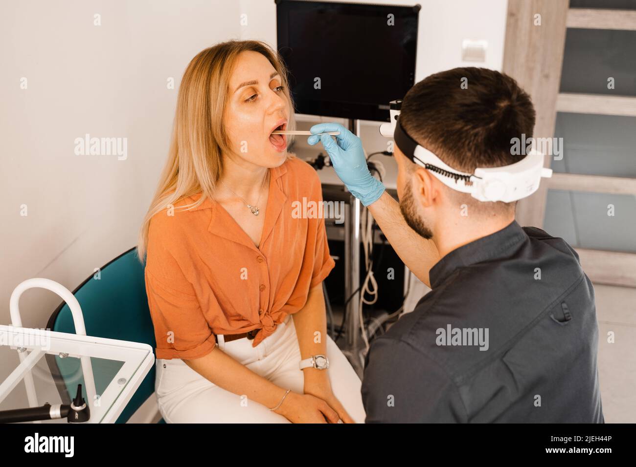 Oropharyngoscopy procedure. Otolaryngologist examines woman throat with ...