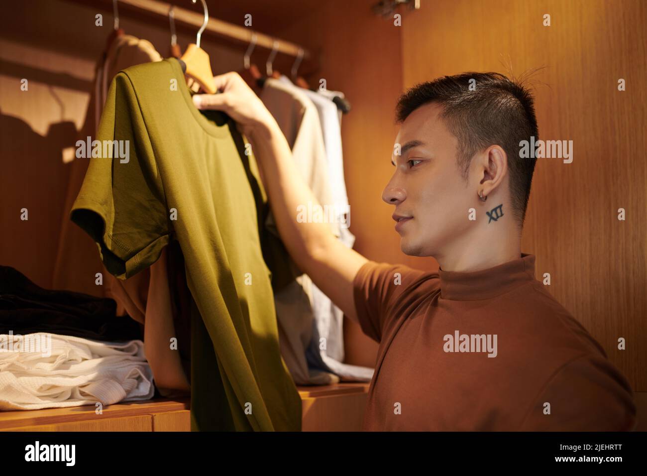 Young man standing in closet and holding hanger with t-short when ...