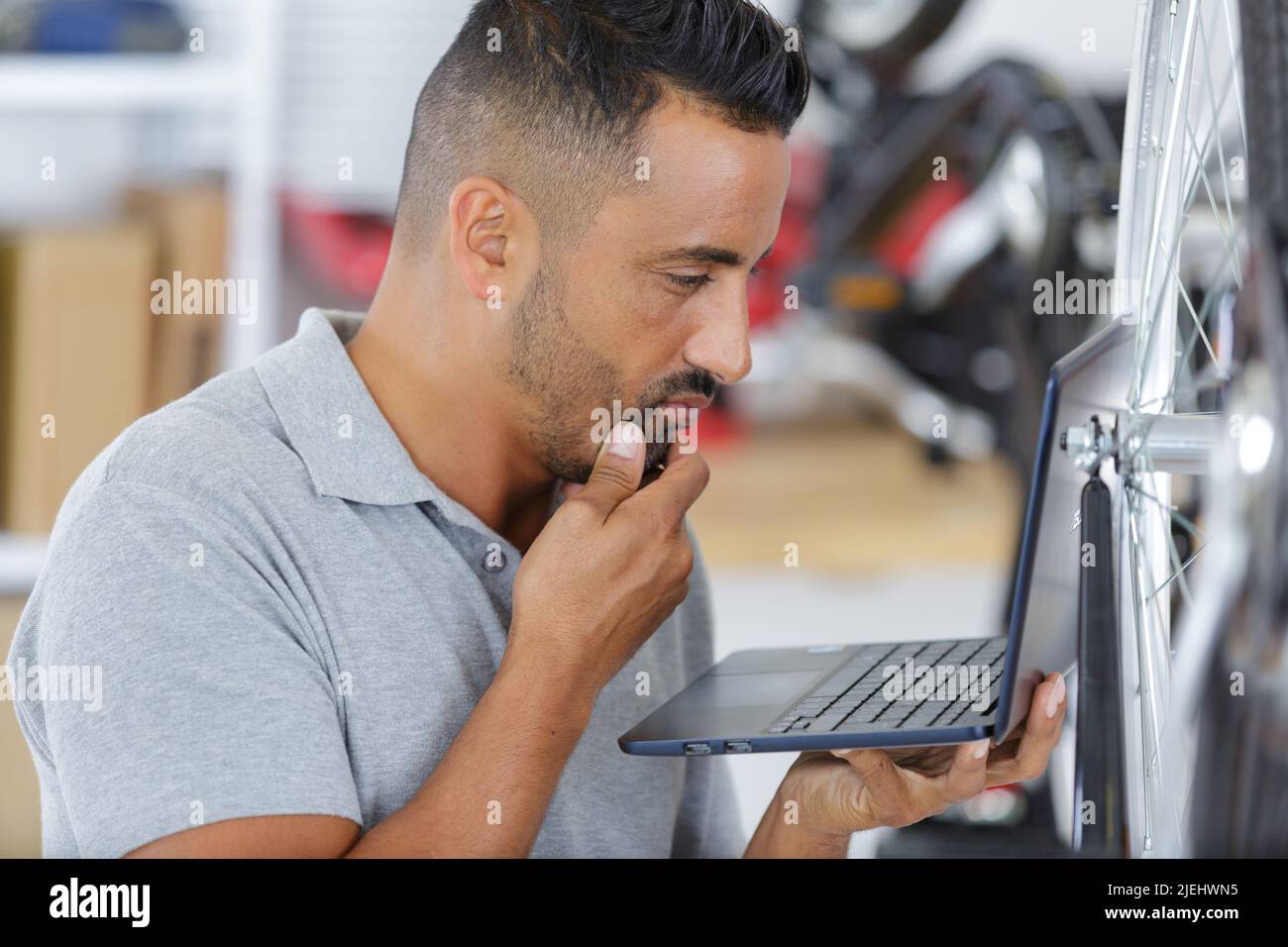 man looking into computer laptop as he fixes his bike Stock Photo - Alamy