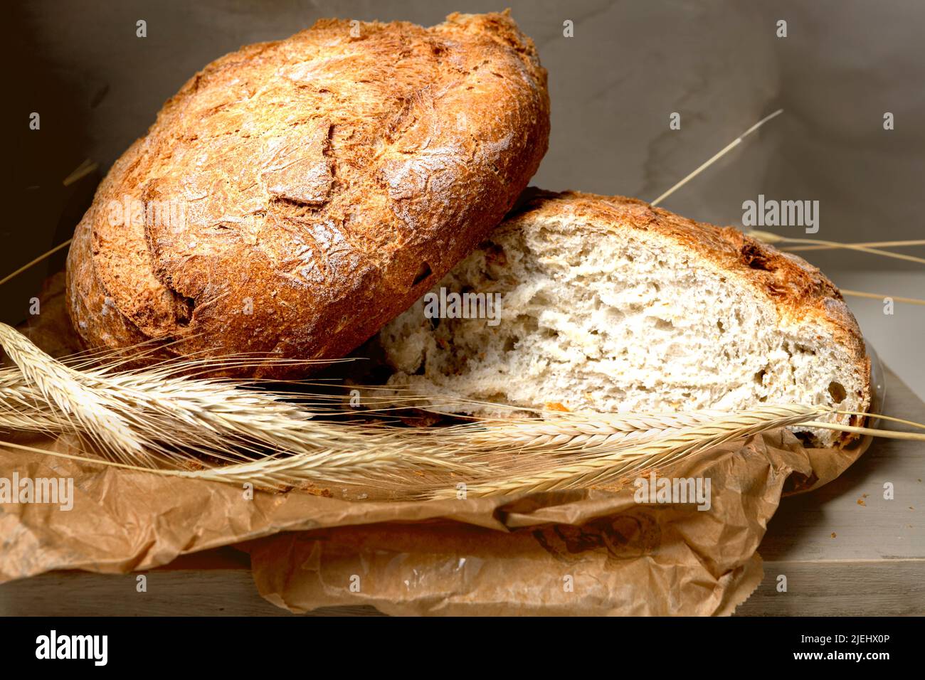 Rustic traditional village bread cut in half on wood with ears of wheat ...