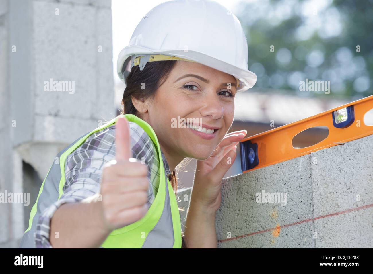 happy female builder with a level shows thumb-up Stock Photo - Alamy