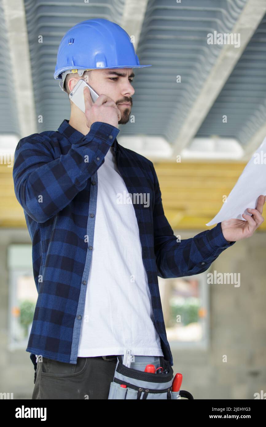 builder with smartphone looking at plans Stock Photo - Alamy