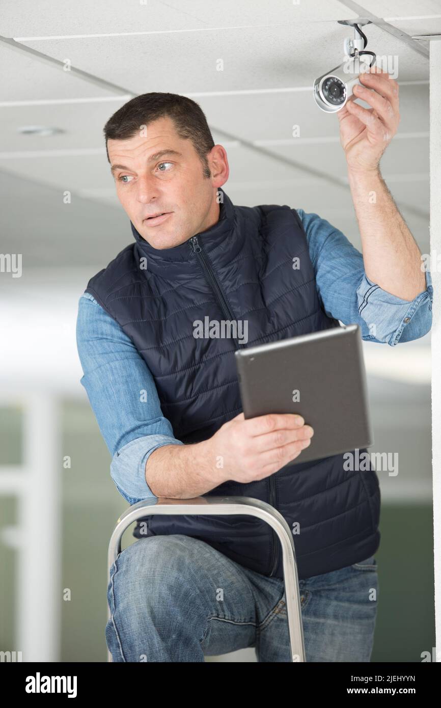 man installing a cctv camera with a tabler Stock Photo - Alamy
