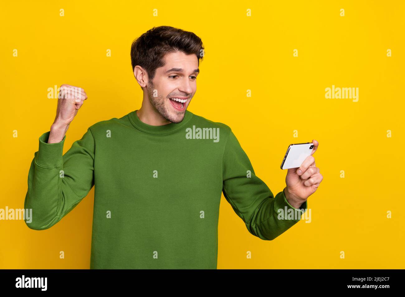 Photo of funky lucky young guy wear green sweater playing modern gadget ...