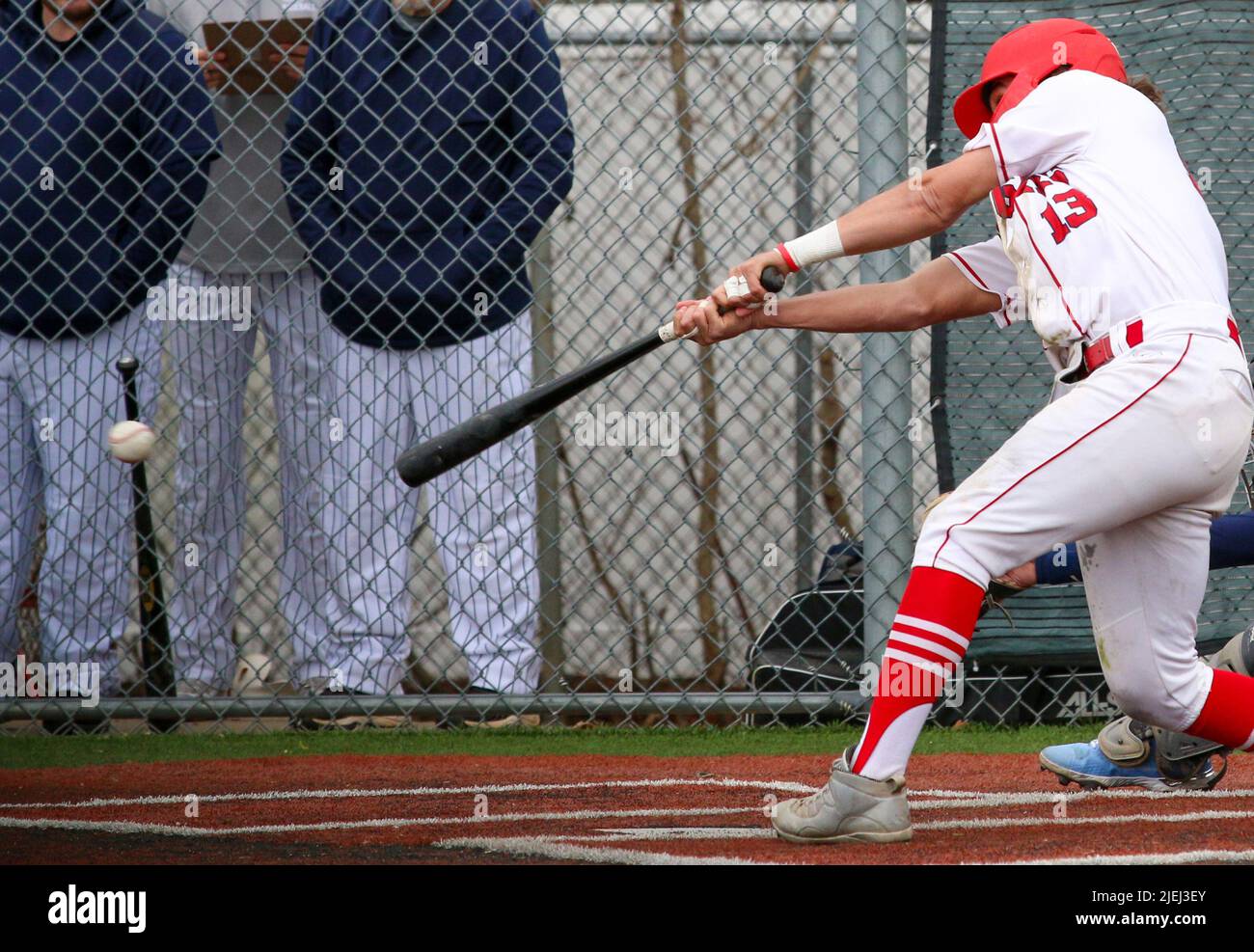 A high school baseball player is swinging at the ball that was just ...