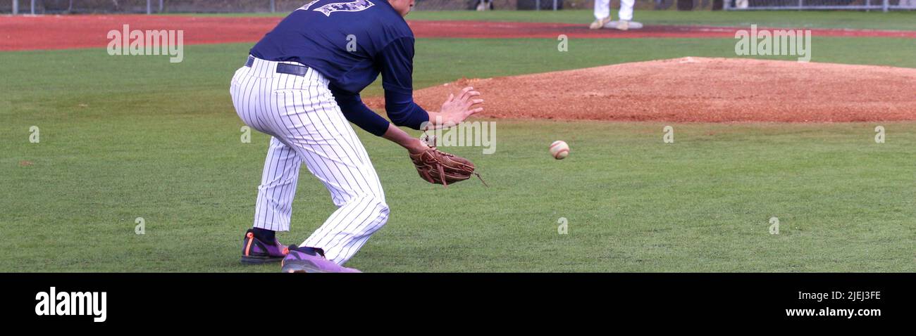 A high school baseball third baseman fielding the ball on the infield ...