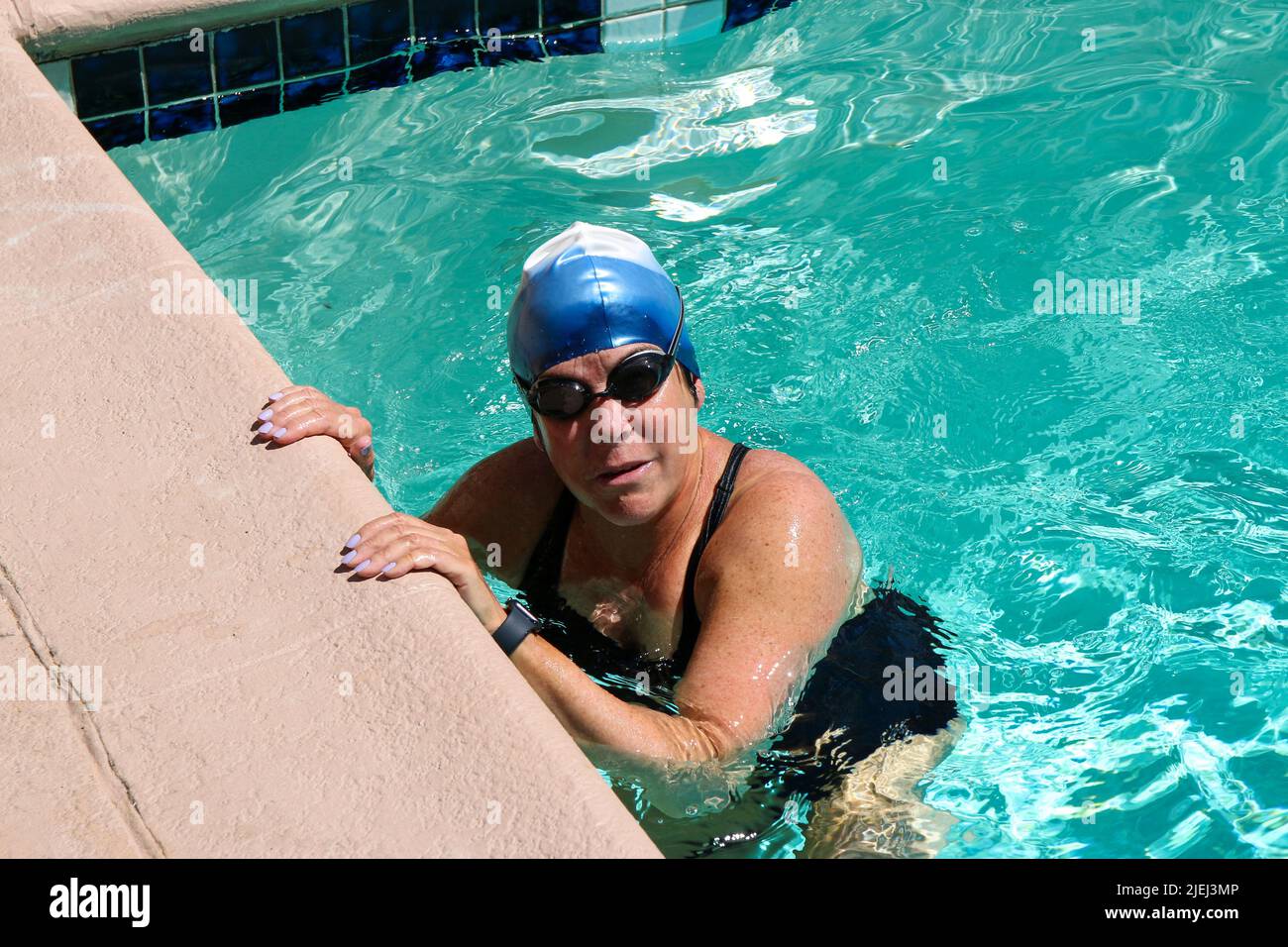A female swimmer taking a break at the edge of an outdoor hotel pool ...