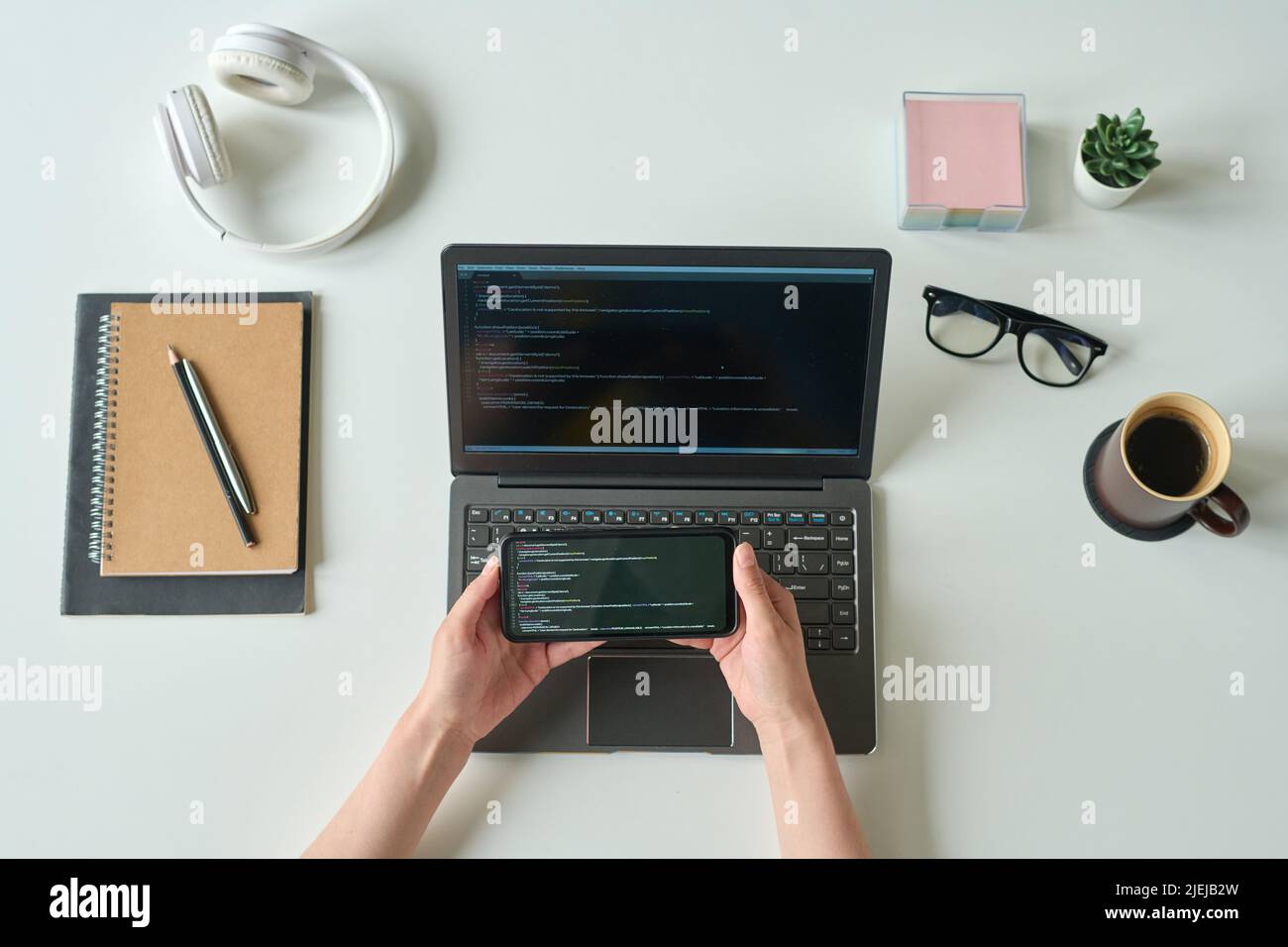 Above view of programmer connecting smartphone with codes with laptop ...