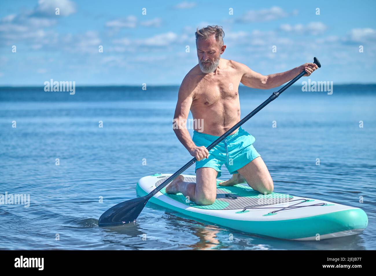Man kneeling on paddle board rowing on water Stock Photo - Alamy