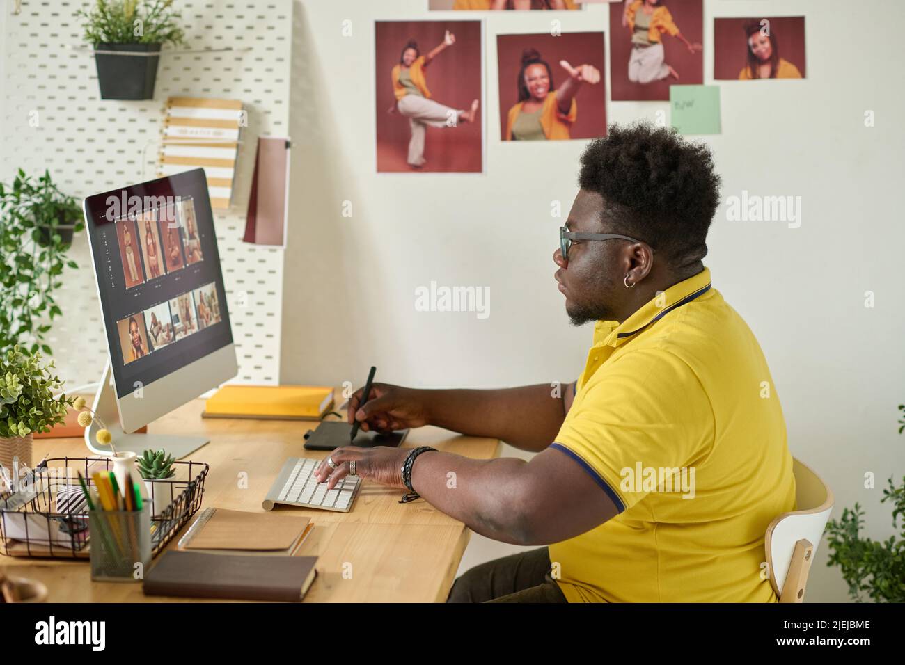 African retoucher sitting at his workplace and using graphic tablet to ...