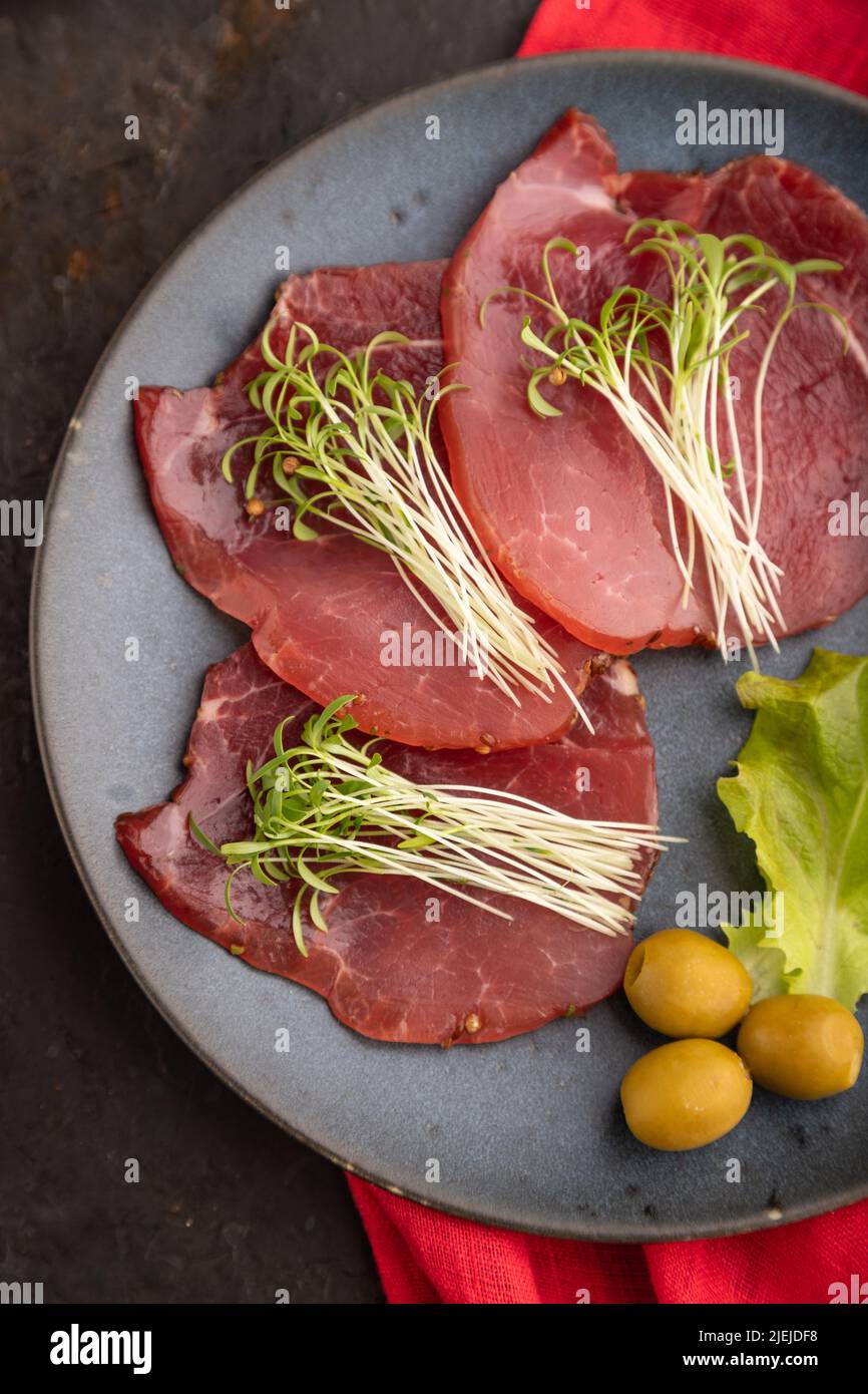 Slices of smoked salted meat with cilantro microgreen on black concrete ...