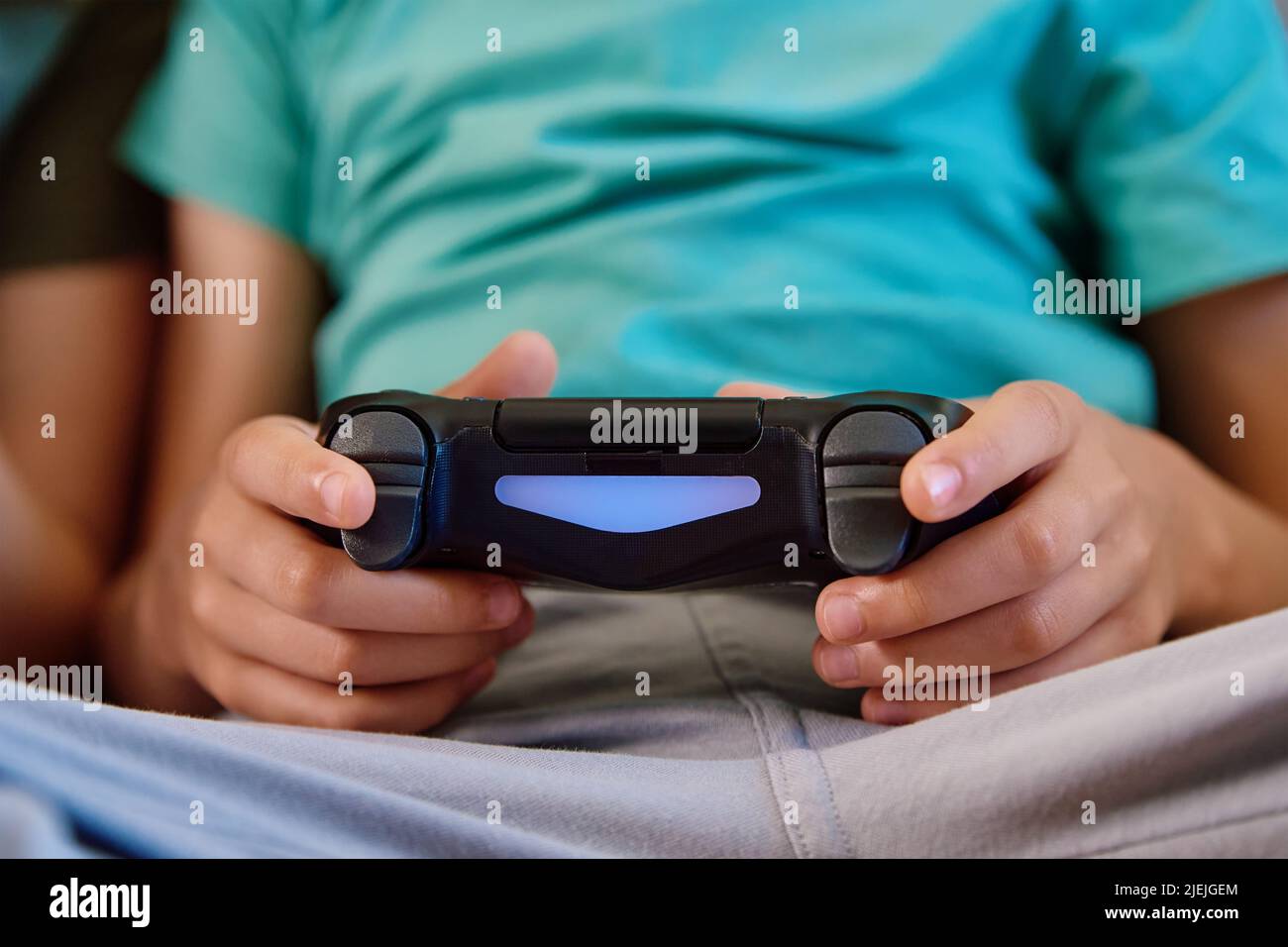 Boy sitting on sofa in living room and playing video game on console ...