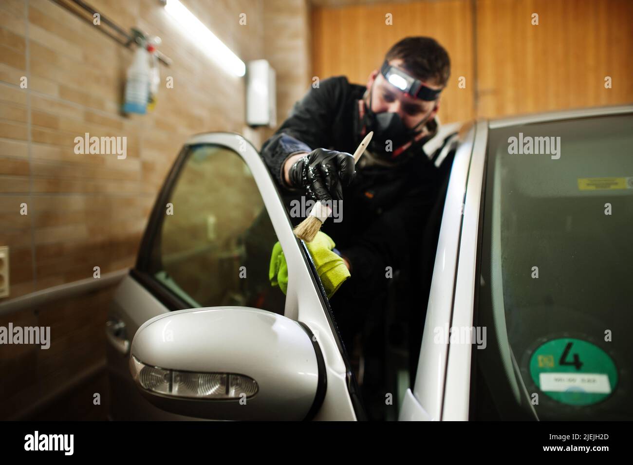 Man in uniform and respirator, worker of car wash center, cleaning car ...