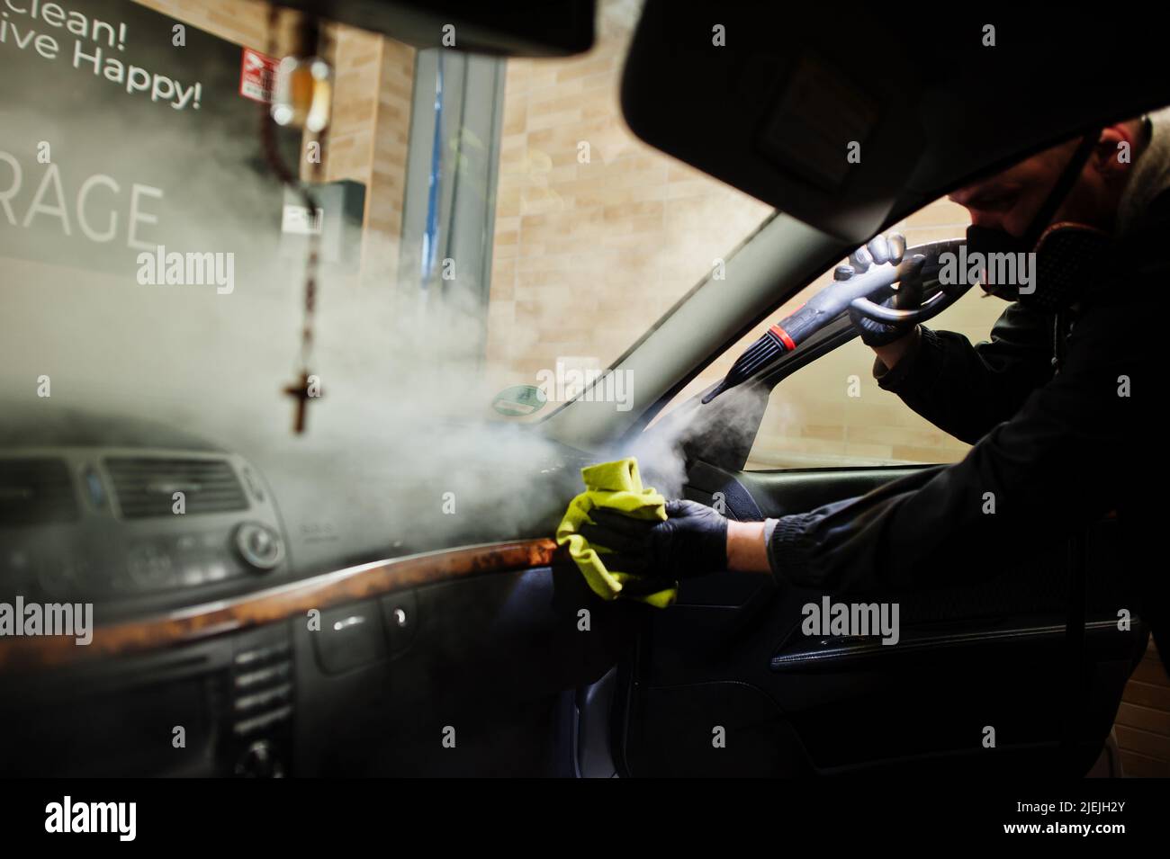 Man in uniform and respirator, worker of car wash center, cleaning car ...
