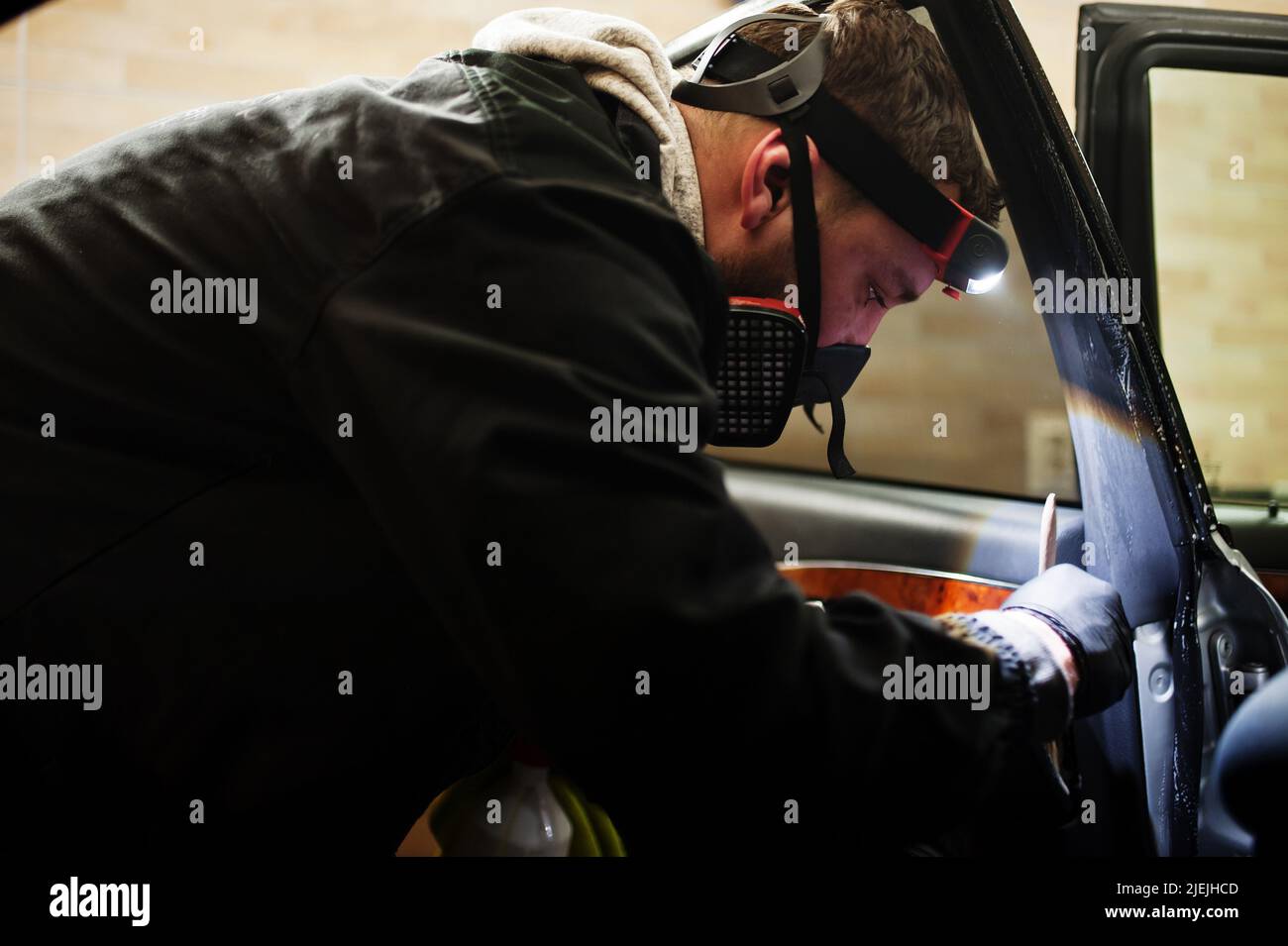 Man in uniform and respirator, worker of car wash center, cleaning car ...