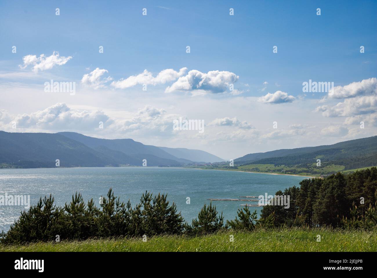 A gleaming wide clear lake reflects bright warm sunlight, against a ...