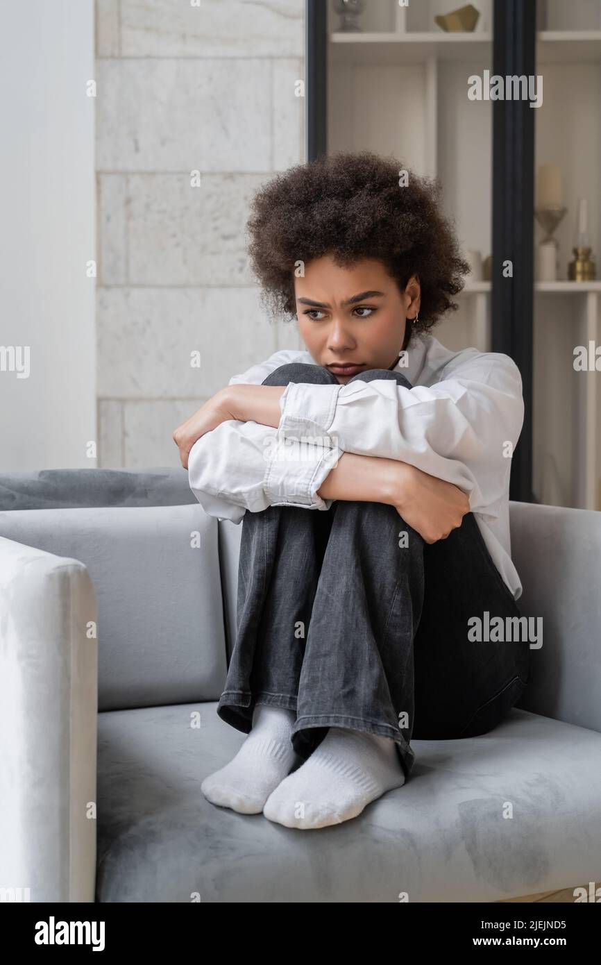 stressed african american woman in white shirt sitting and hugging legs ...