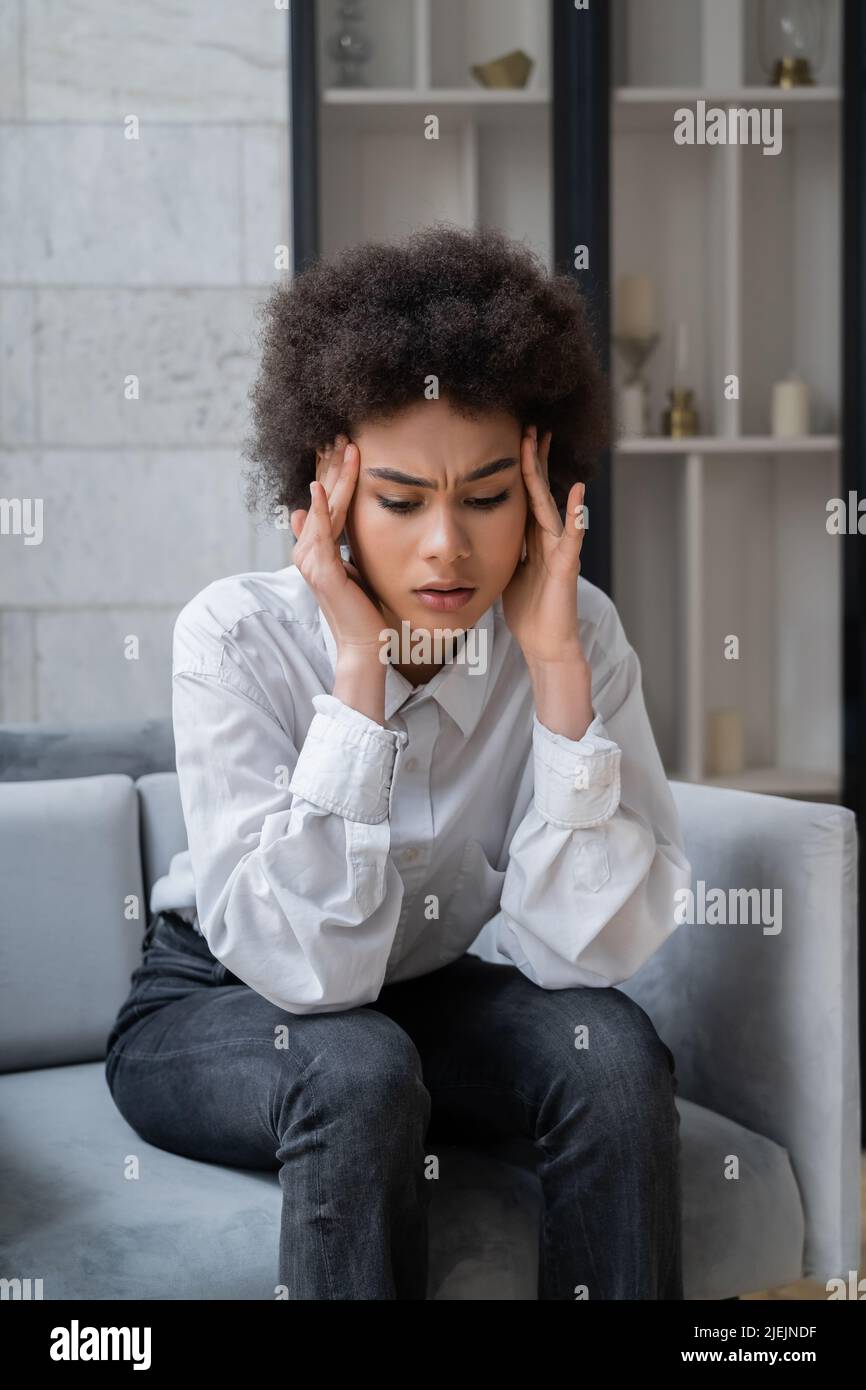 stressed african american woman in white shirt sitting in living room ...