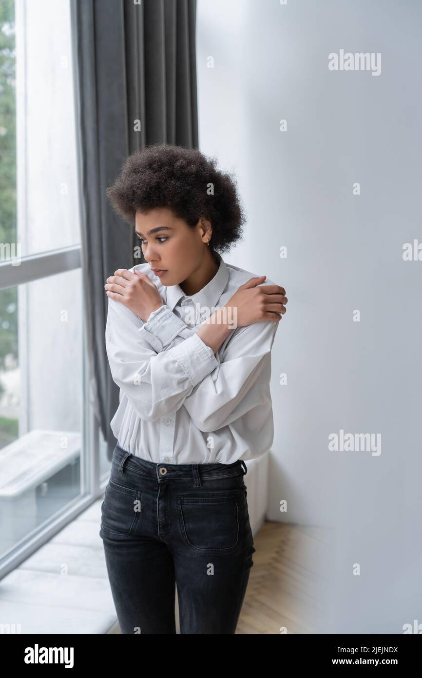 depressed african american woman in white shirt and jeans hugging ...