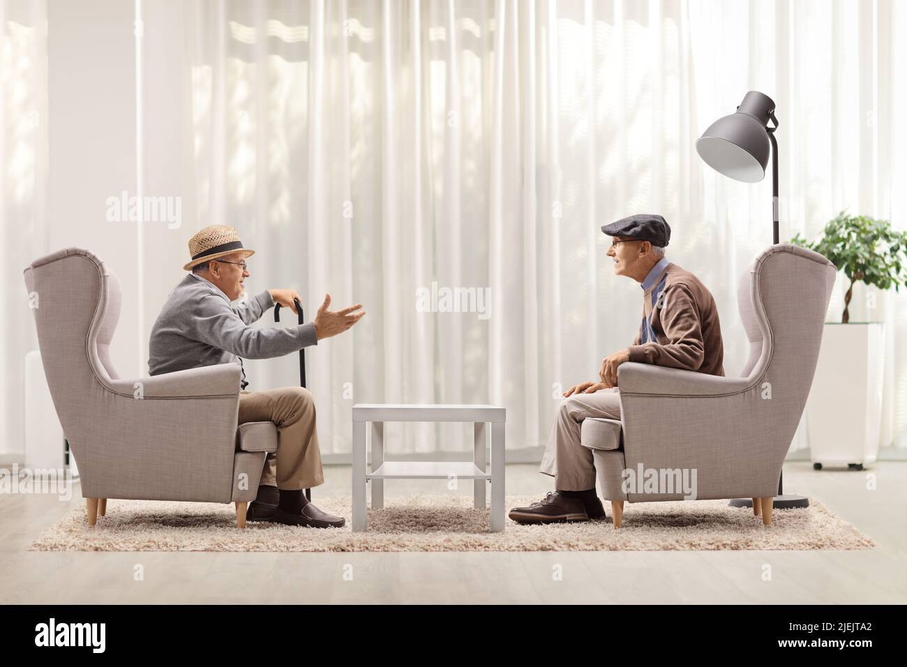 Two elderly men seated in armchairs having a conversation in a room ...
