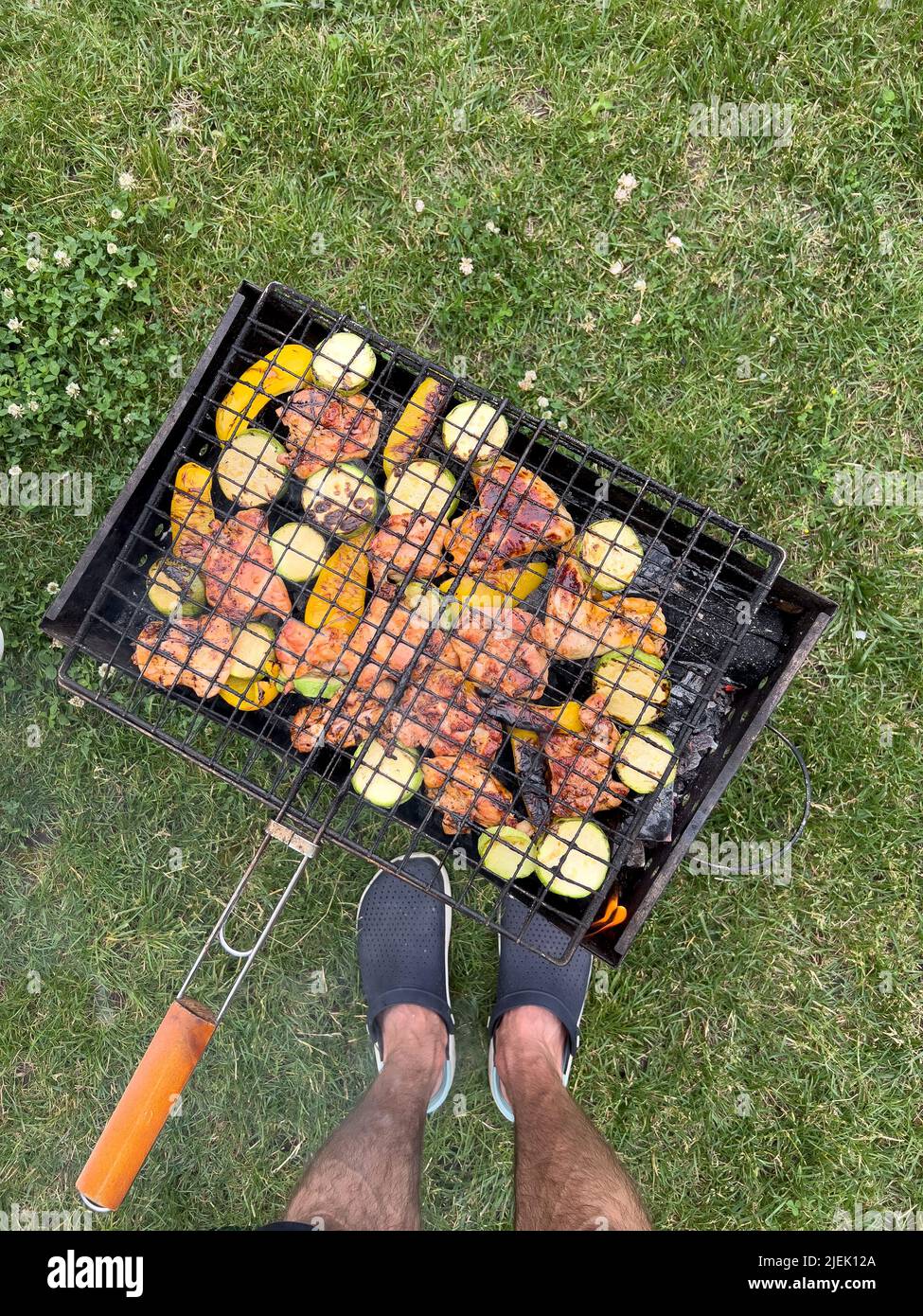 Legs of man in shoes are near lattice on grill with meat steaks and ...