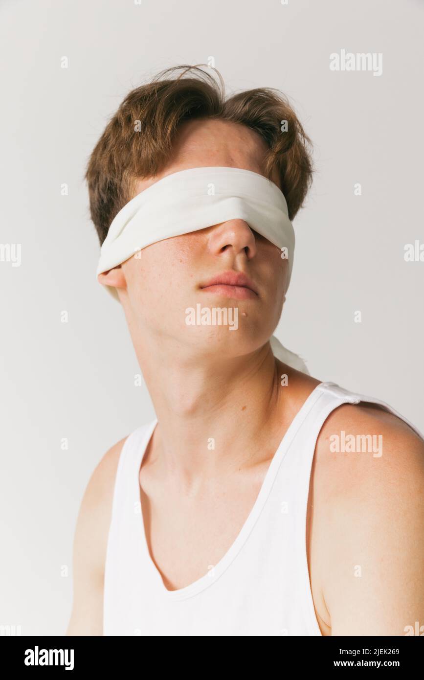 Portrait of young man with blindfold sitting on chair isolated on white ...