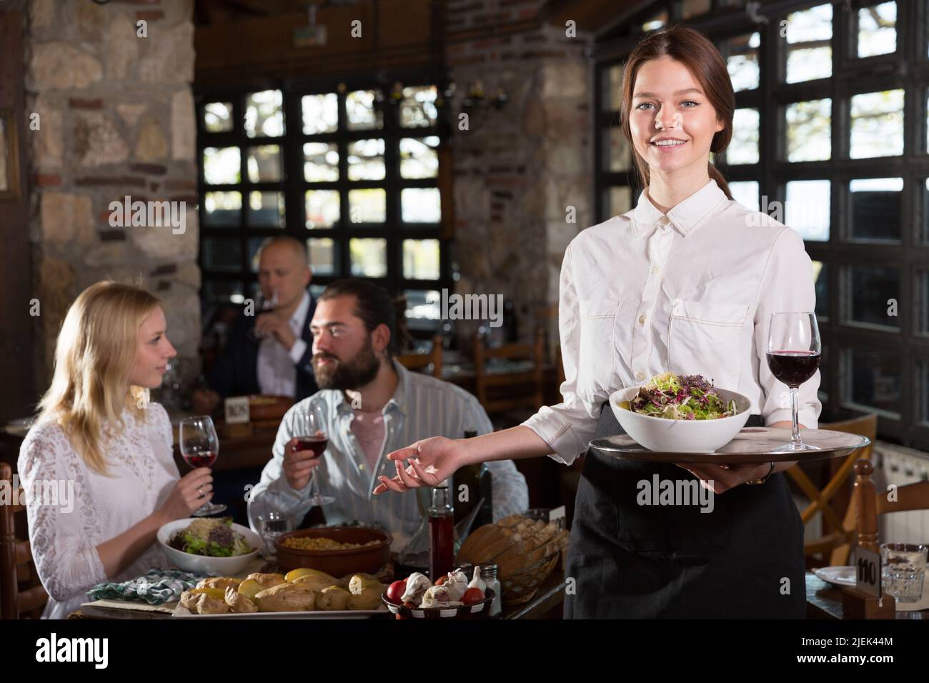 Positive woman waiter demonstrating country restaurant to visitors ...