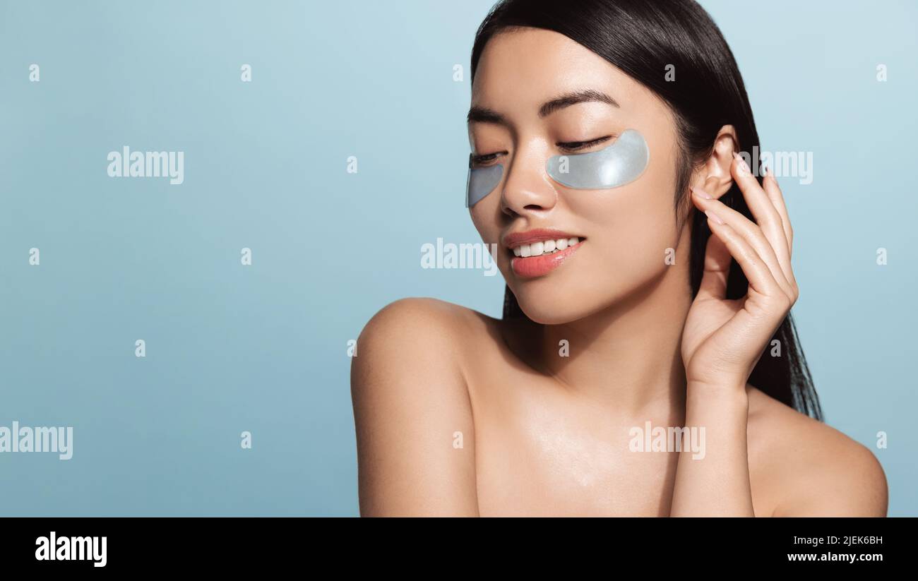 Beautiful young asian woman, uses under eye patches, tuck hair behind ...