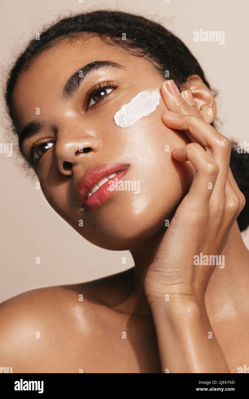 Vertical of beauty woman, dark skinned model applies facial cream ...