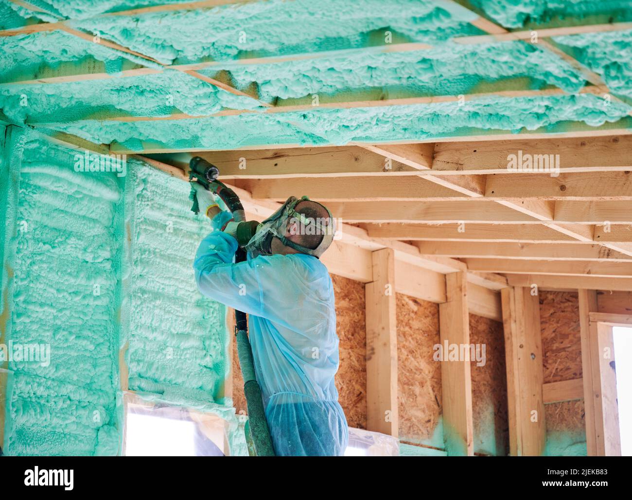 Male builder insulating wooden frame house. Man worker spraying ...