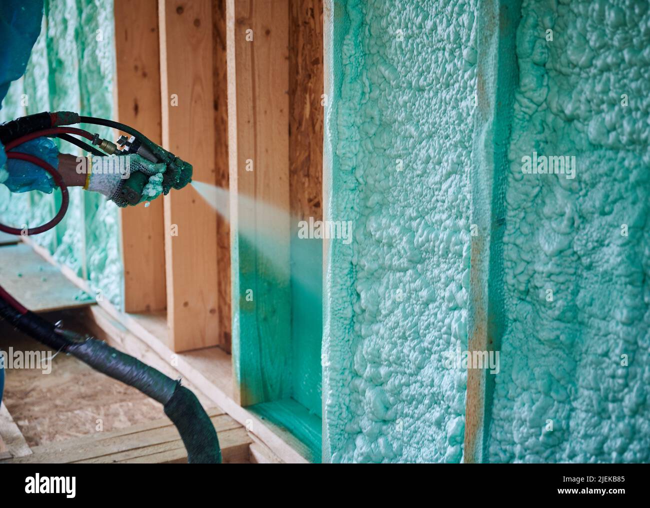 Builder insulating wooden frame house. Close up view of man worker spraying polyurethane foam ...