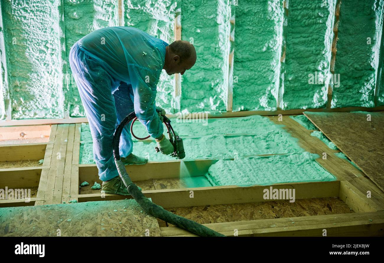 Male builder insulating wooden frame house. Man worker spraying ...