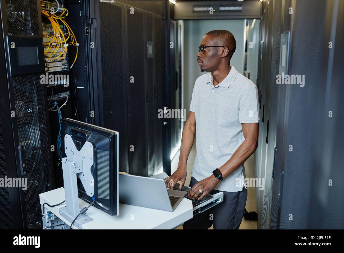 Side view portrait of black man connecting laptop to server cabinet and ...