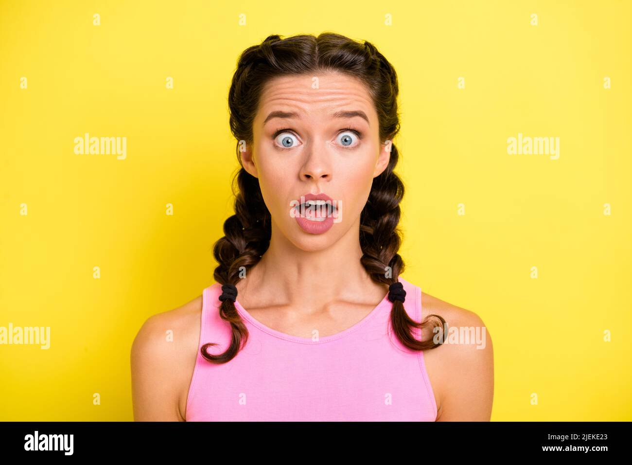 Photo of charming impressed young woman pigtails wear tank top big eyes ...