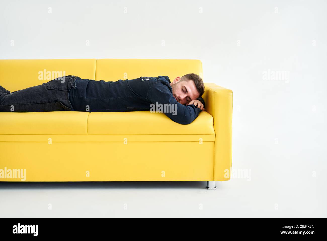 Tired young man lying down on yellow sofa over white background ...