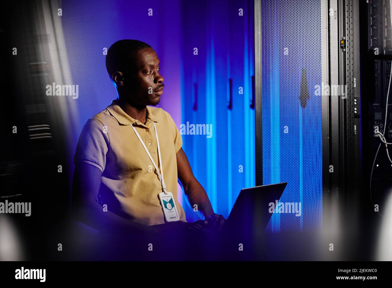 Side view portrait of adult black man using laptop in dark server room ...