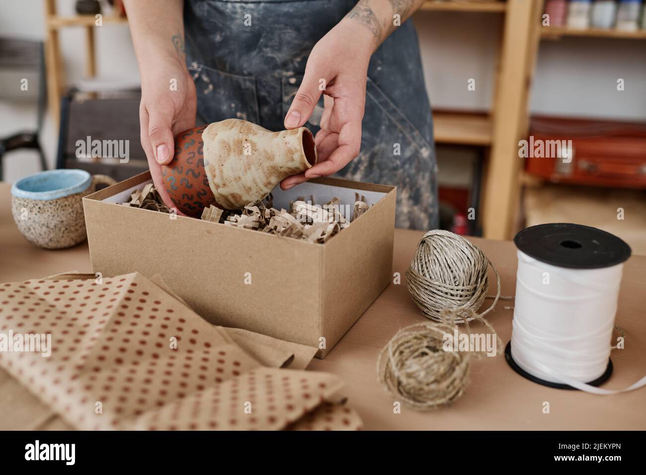 Young female pitcher or owner of small pottery shop putting clay jug ...