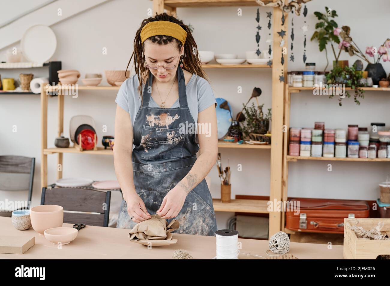 Young woman in workwear tying wrapped and packed earthenware item ...