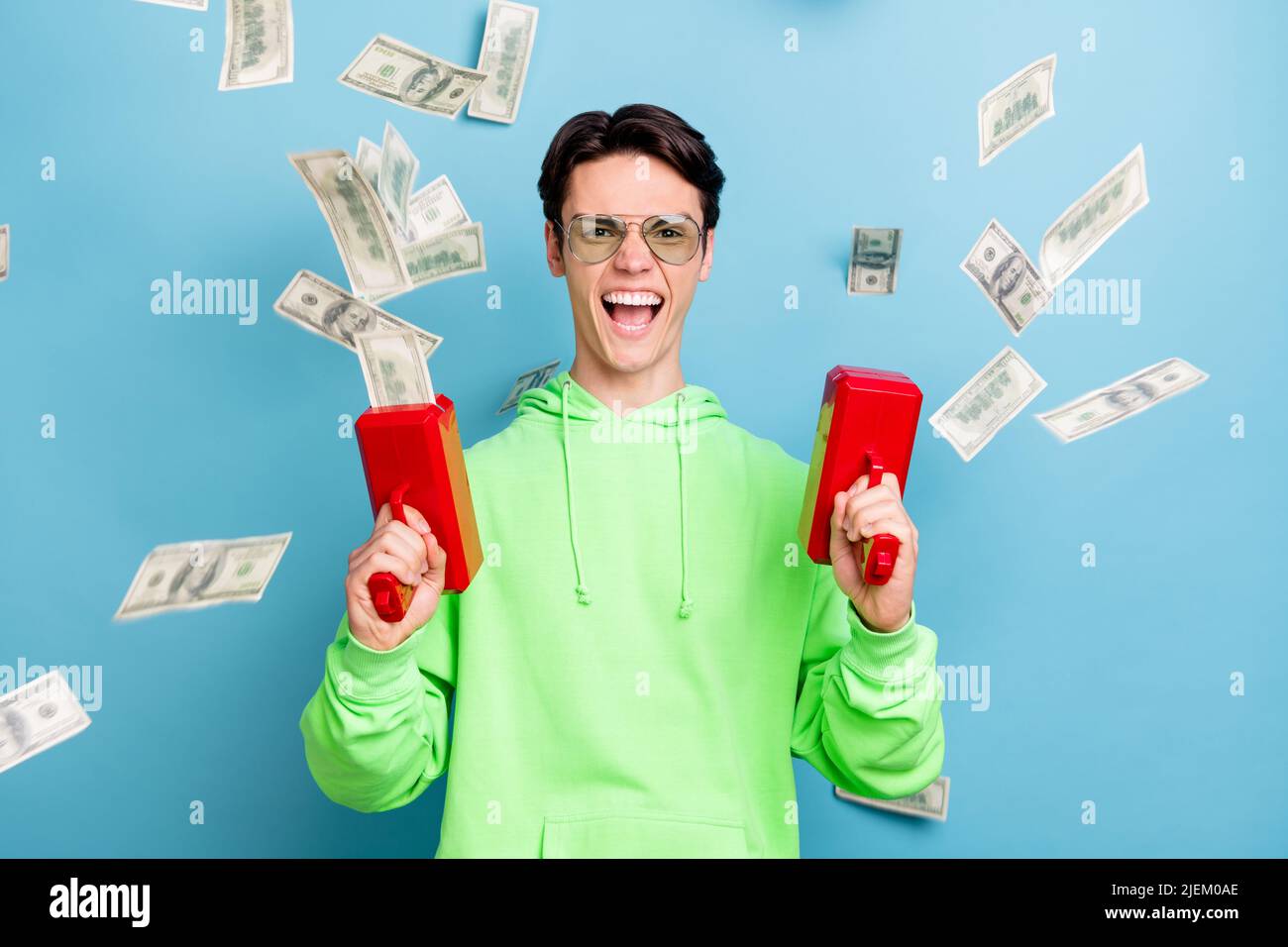 Photo of funky cool young guy dressed green hoodie shooting money gun ...