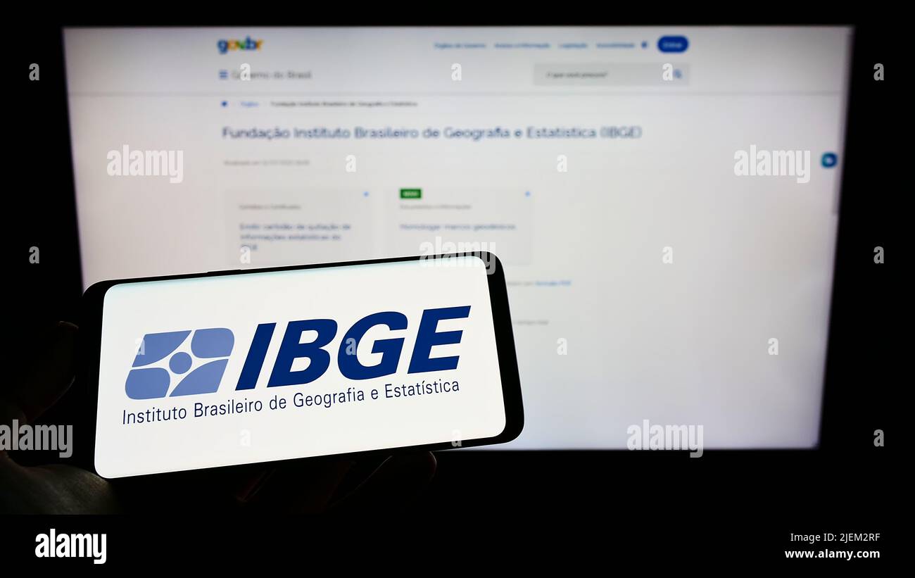 Person holding mobile phone with logo of Instituto Brasileiro de ...