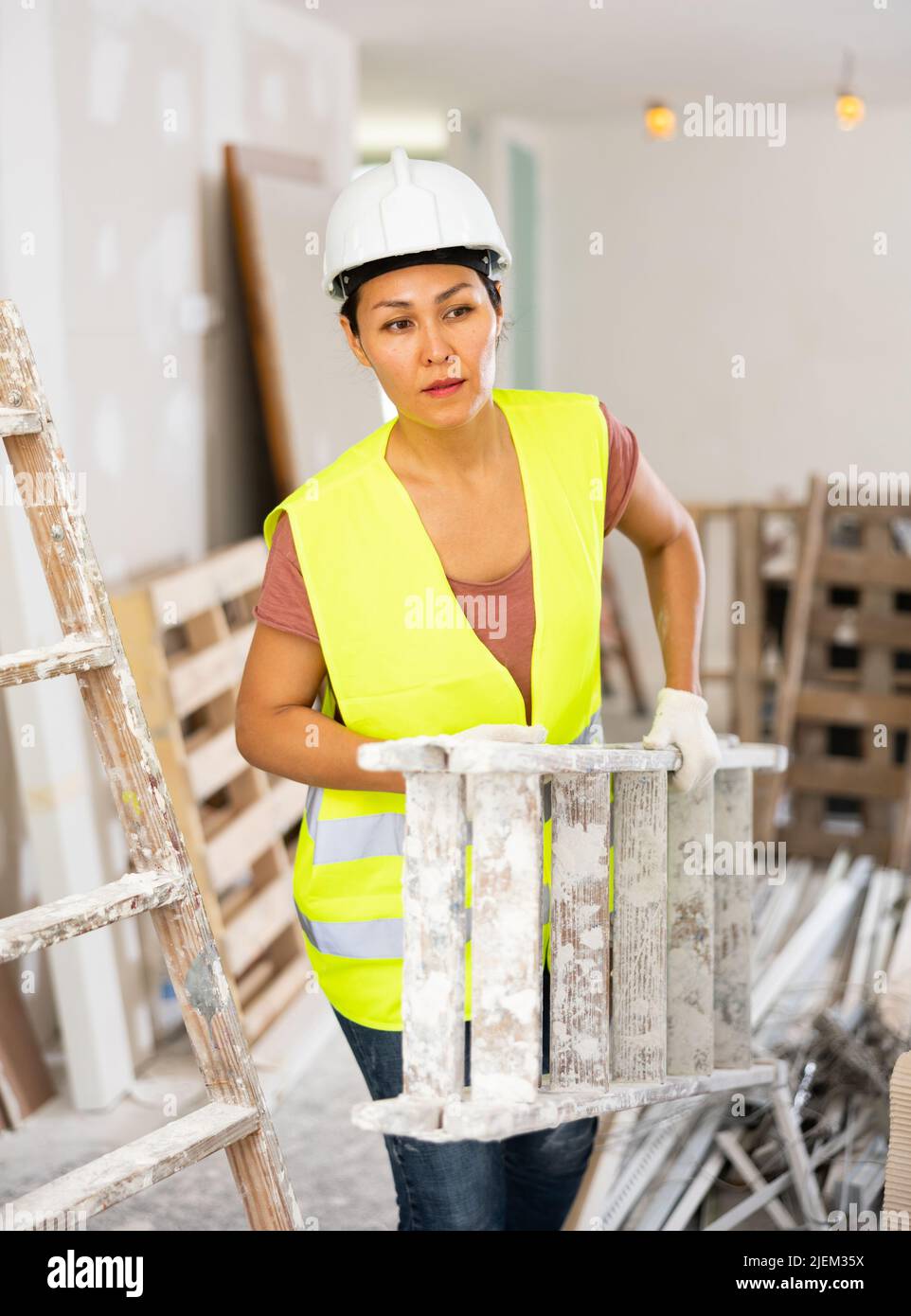 Female construction worker carrying ladder during renovation works ...