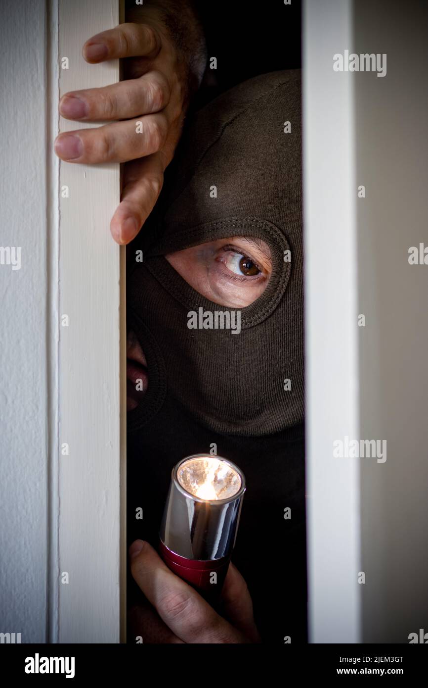 A criminal with a mask on his face opens the door to the room Stock ...