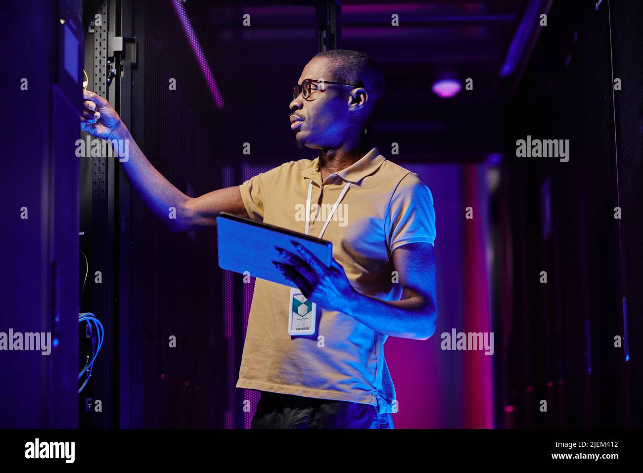 Side view of male system administrator setting up server network in data center lit by neon ...