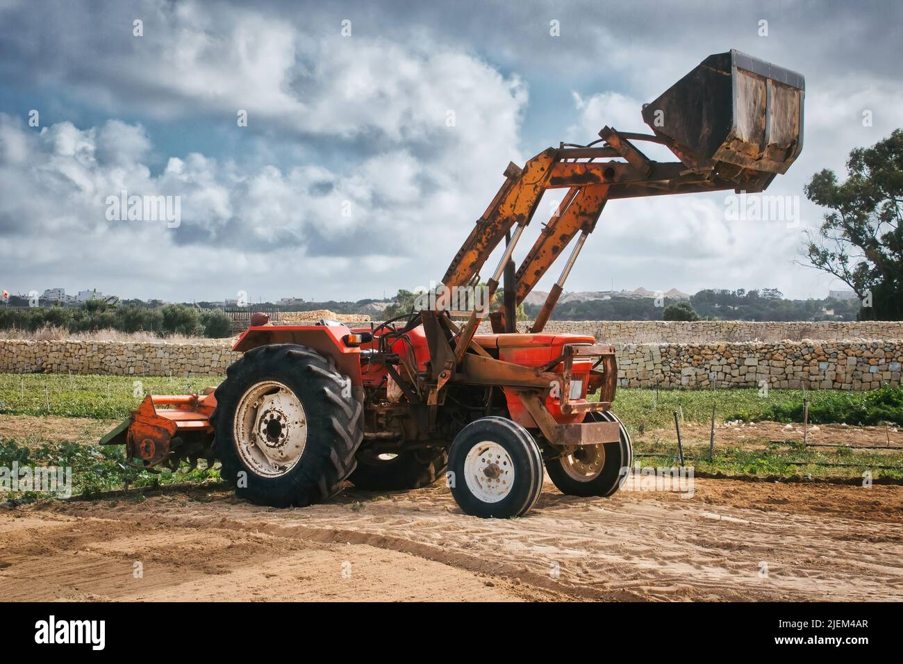 Agricultural tractor with digger and ploughing attachment at the back ...