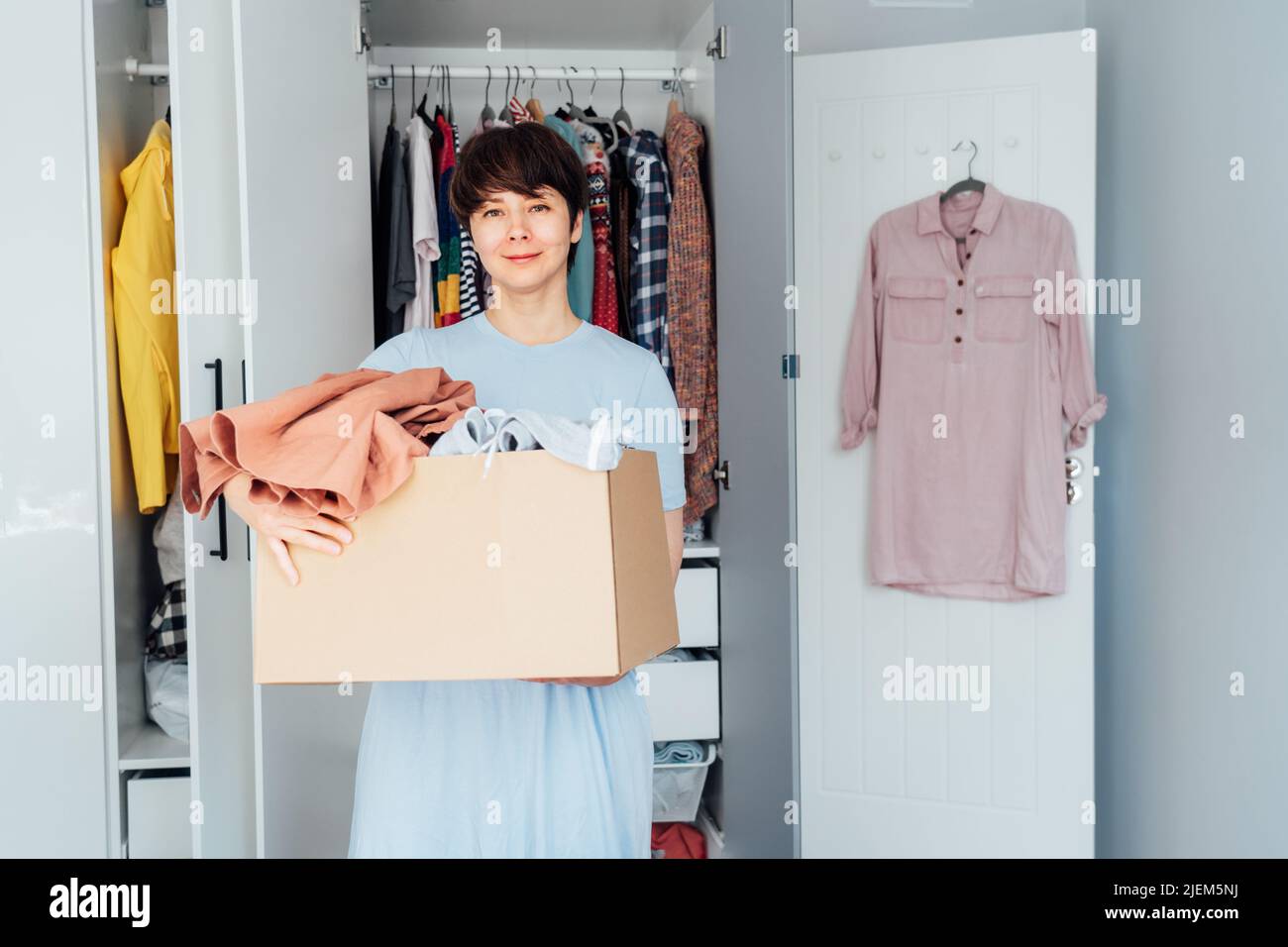 Smiling Woman With Box Of Selected Clothes From Her Wardrobe For Donating To A Charity