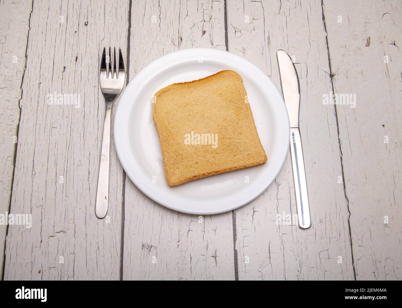 A single slice of toast on a plain white plate and cutlery with signs ...