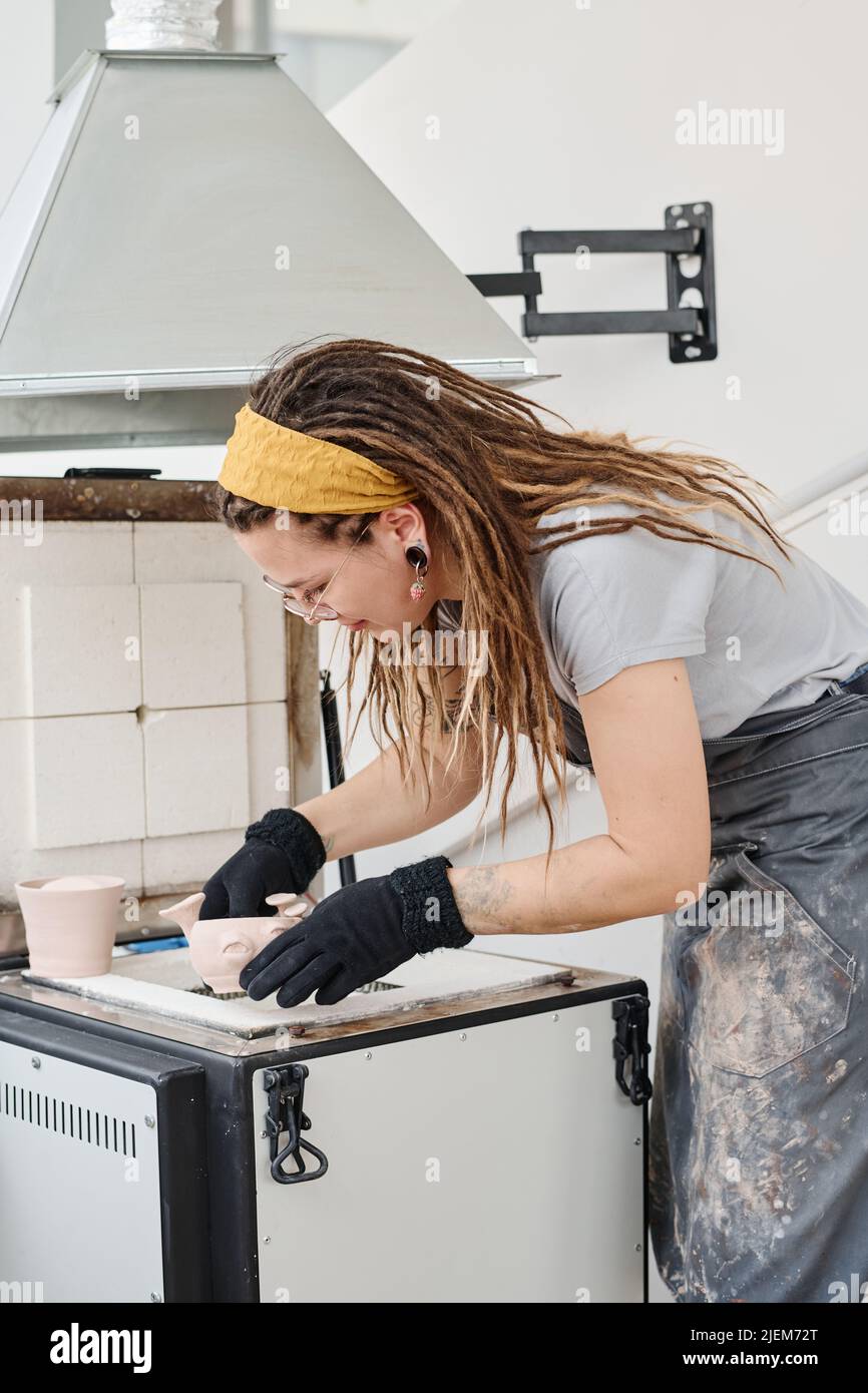Young creative woman in workwear and protective thick black gloves ...