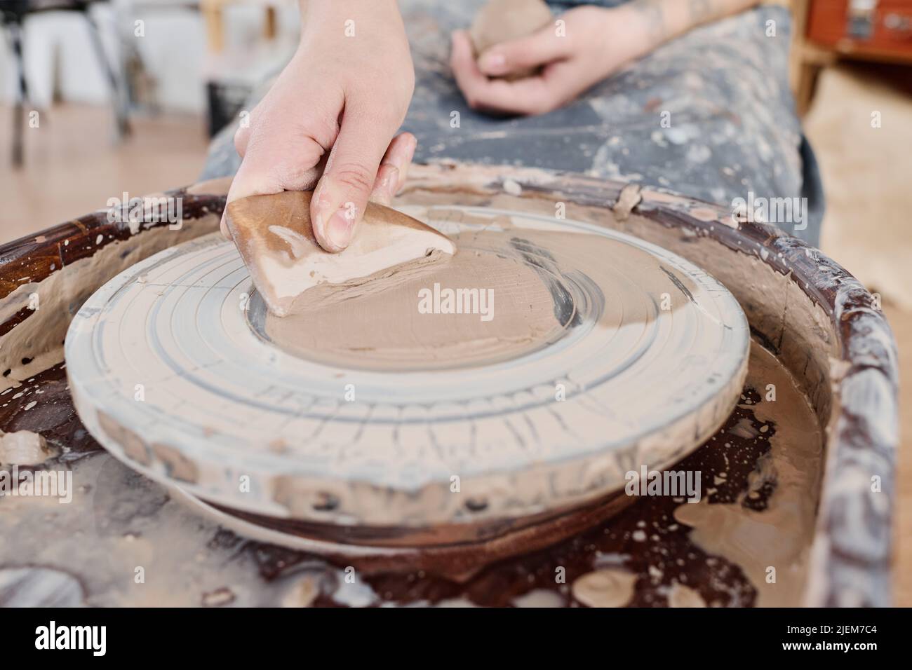 Hand of young creative female potter applying clay on rotating pottery ...