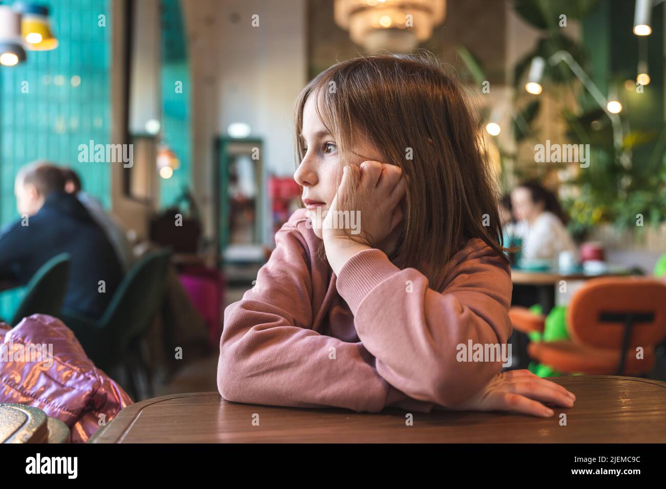 a cute brooding girl sits at a table in a cafe and looks out the window ...