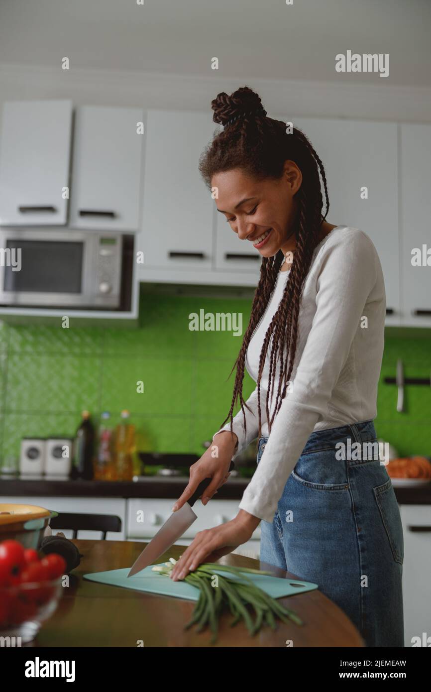 Vertical shot of cheerful young pretty female cooking in kitchen at ...
